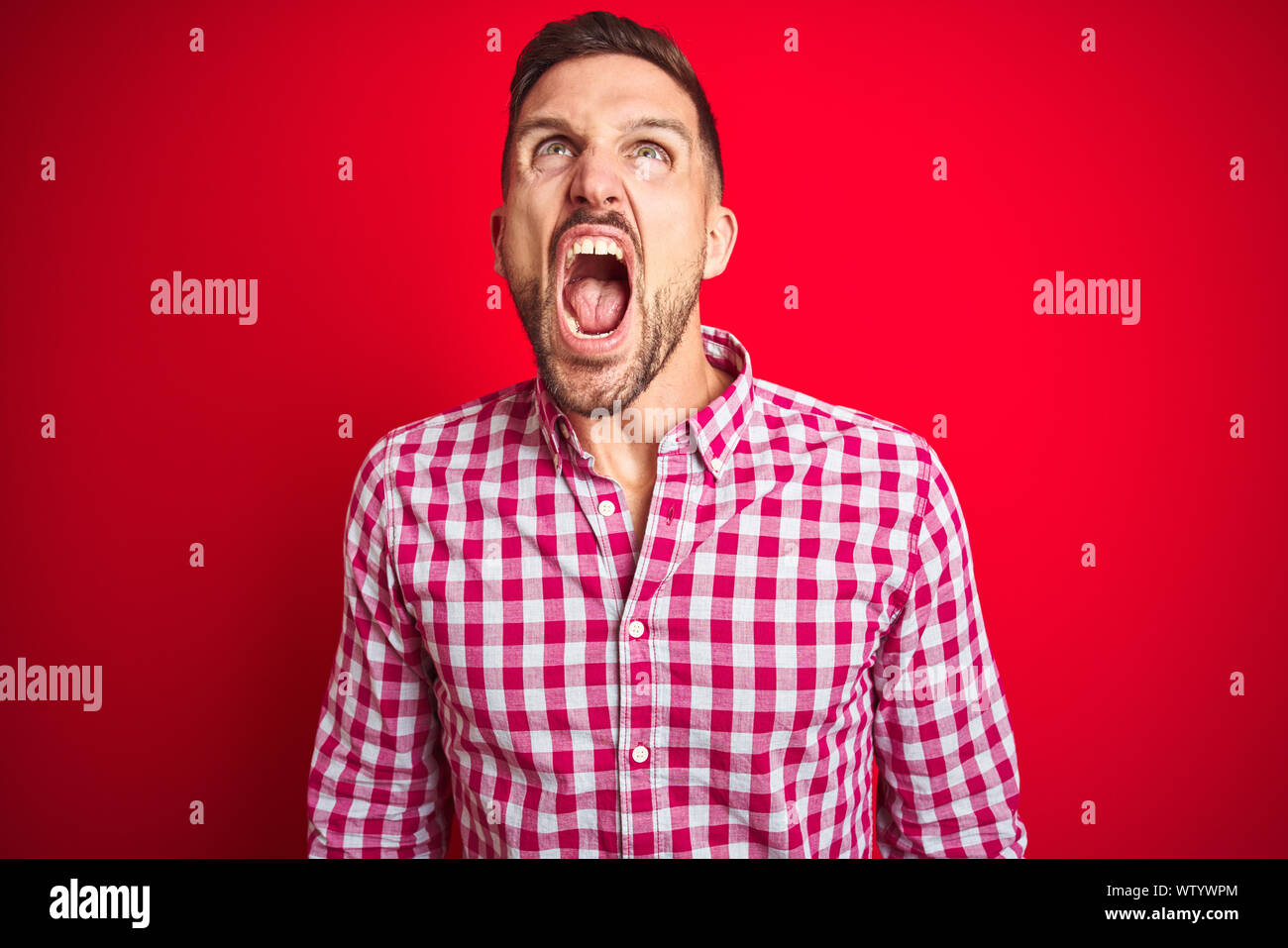 Young handsome man over red isolated background angry and mad screaming ...