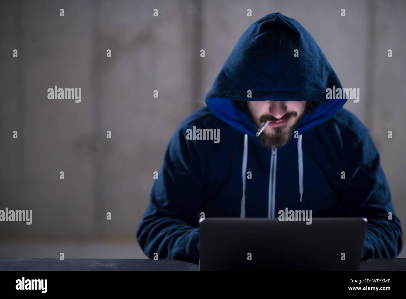 Young talented hacker smoking cigarette while working on laptop ...
