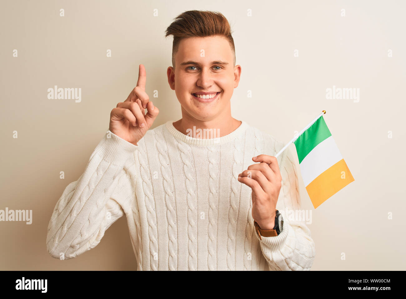 Young handsome man holding Ireland Irish flag over isolated white ...