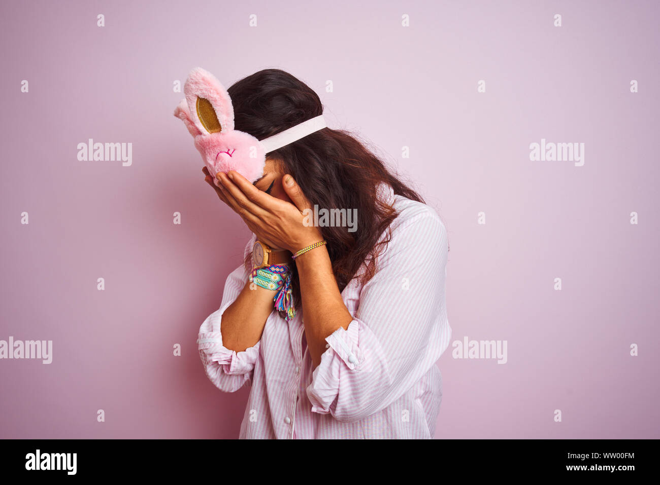 Young beautiful woman wearing pajama and sleep mask over isolated pink ...