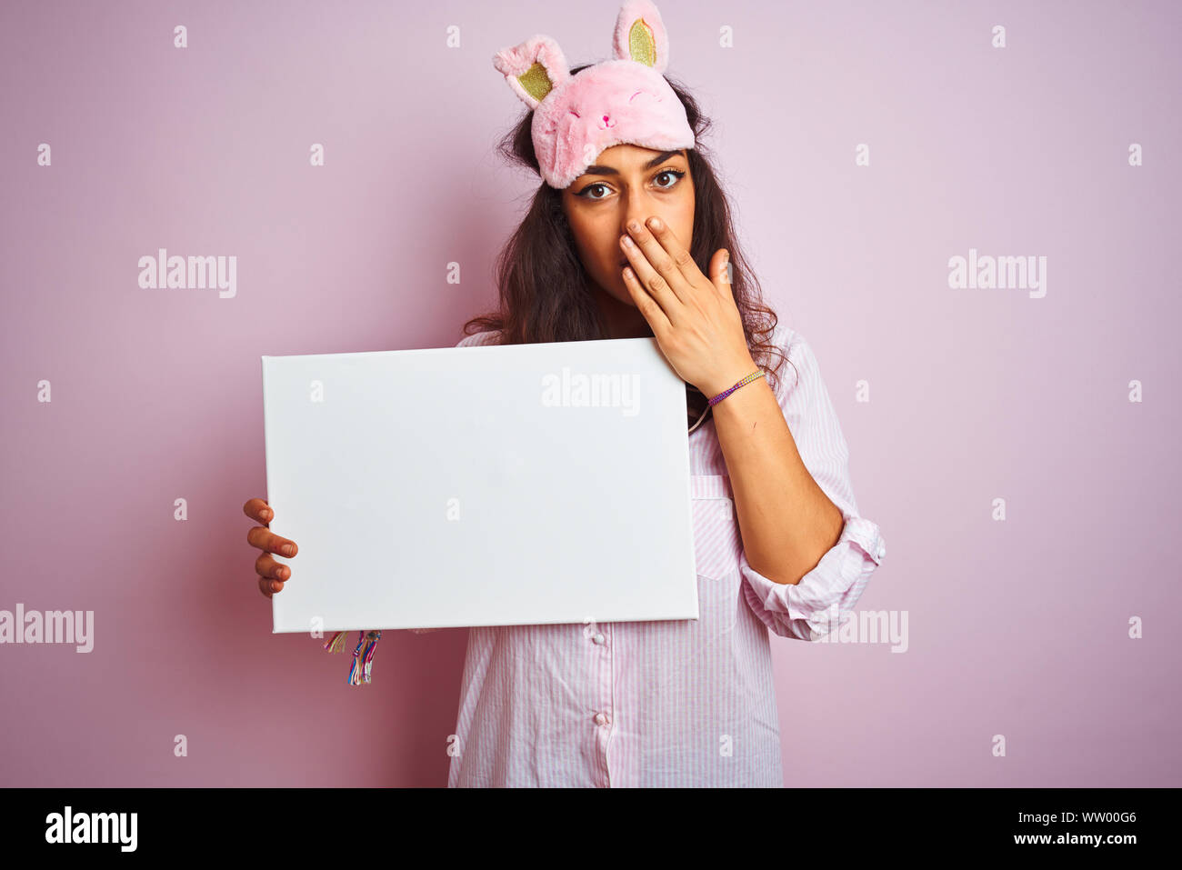 Young woman wearing pajama and sleep mask holding banner over isolated ...
