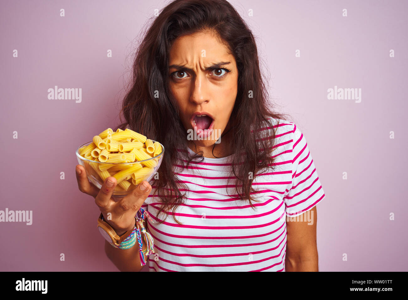 Young beautiful woman holding bowl with dry macaroni pasta over ...