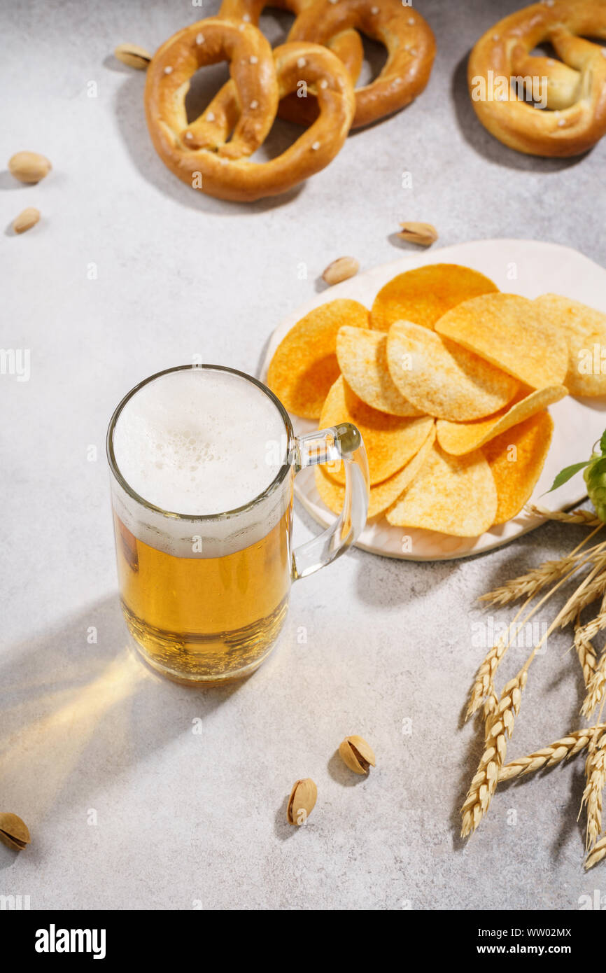 A mug of lager beer with german pretzels and chips on a light gray ...