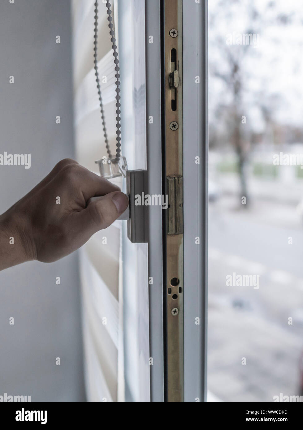 Man holding window handle on a plastic window with white fabric roller ...