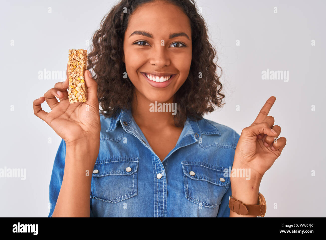 Young brazilian woman eating granola bar standing over isolated white ...