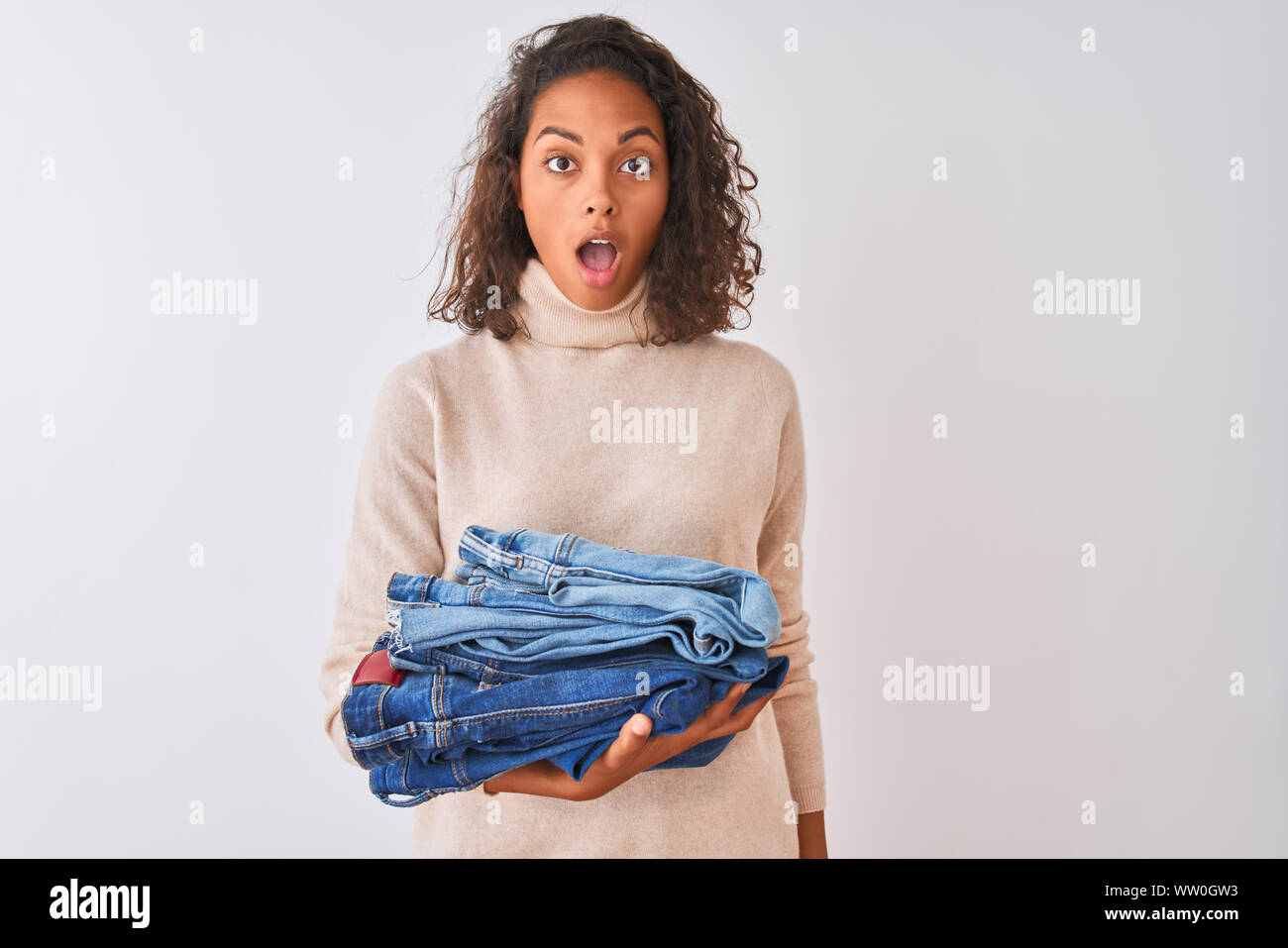 Young brazilian shopkeeper woman holding pile of jeans over isolated ...