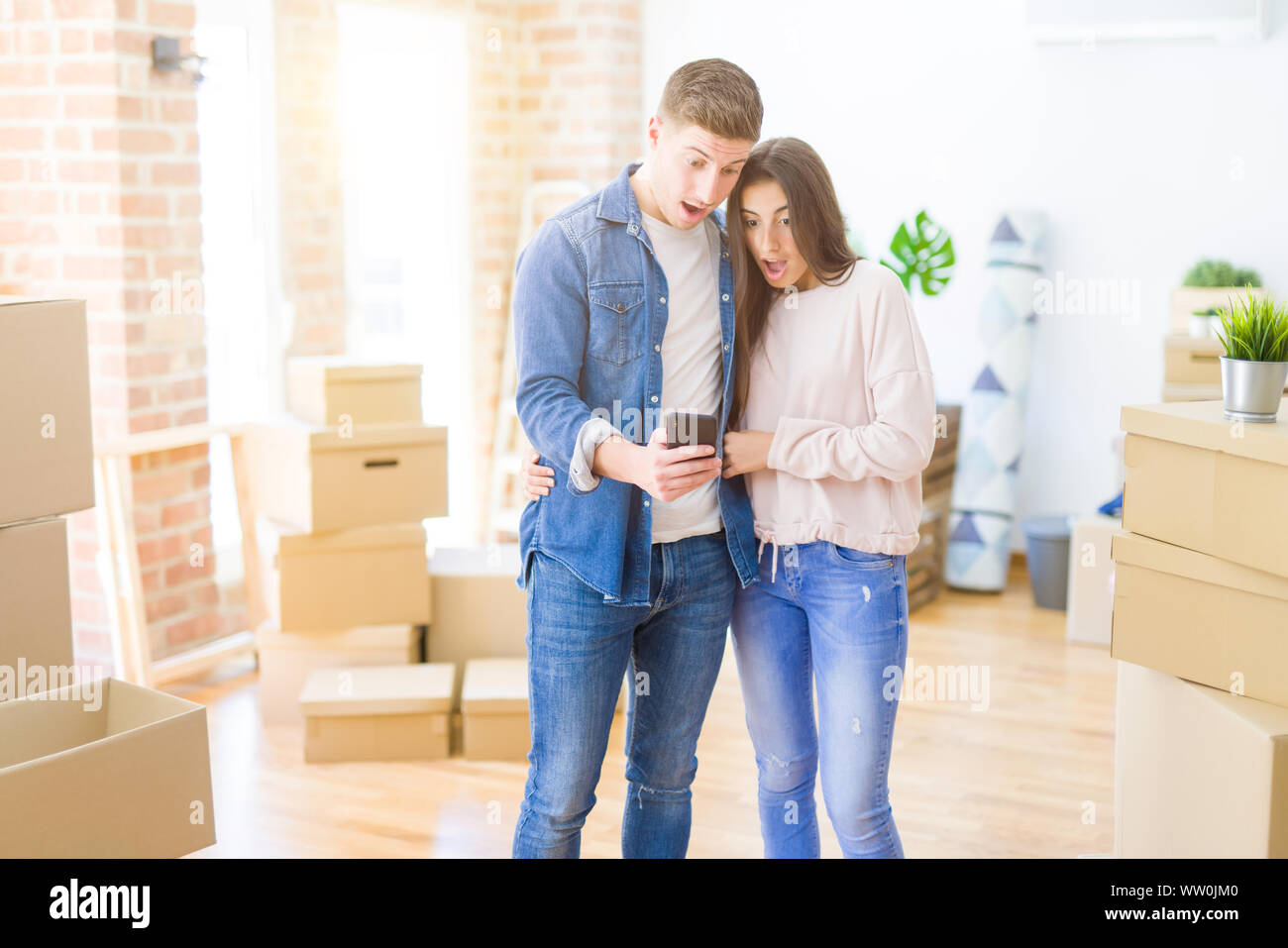 Beautiful young couple moving to a new house using smartphone scared in ...