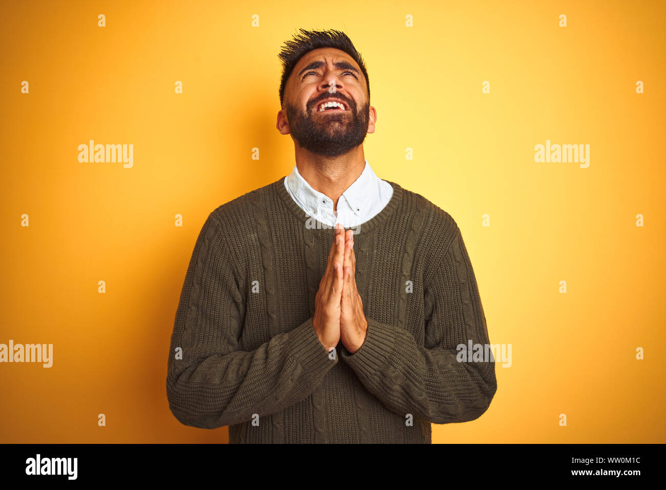 Young indian man wearing green sweater and shirt standing over isolated ...