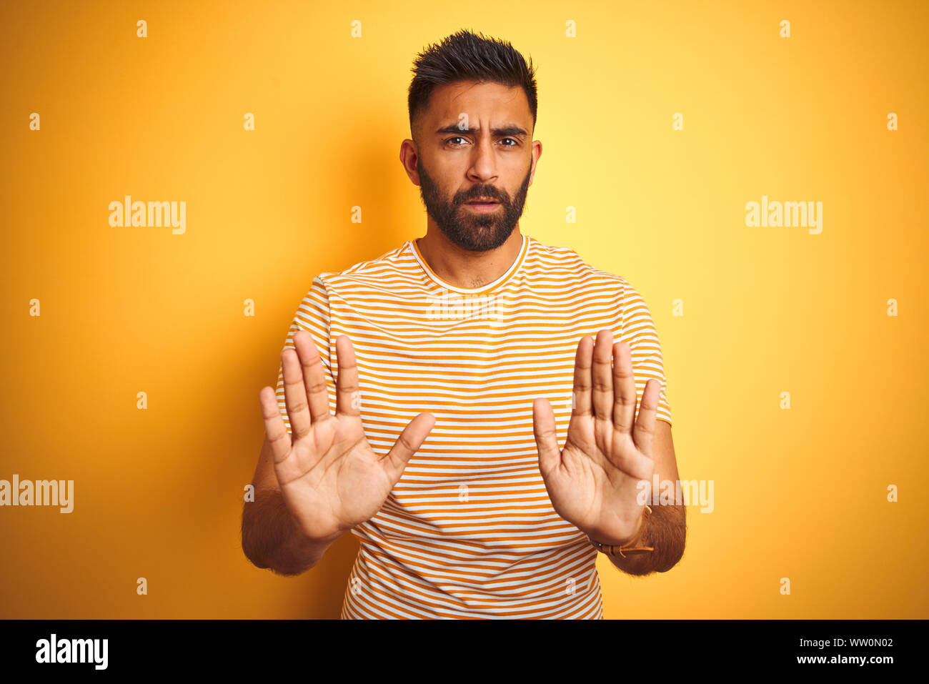 Young indian man wearing t-shirt standing over isolated yellow ...