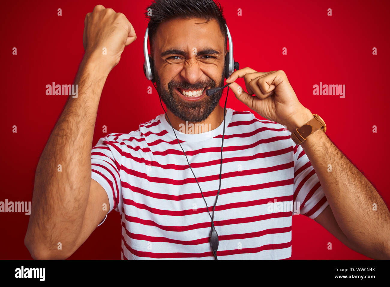 Young indian call center agent man using headset over isolated red ...