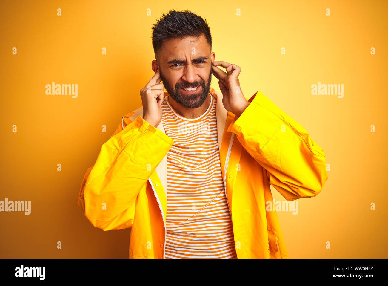 Young indian man wearing raincoat standing over isolated yellow ...
