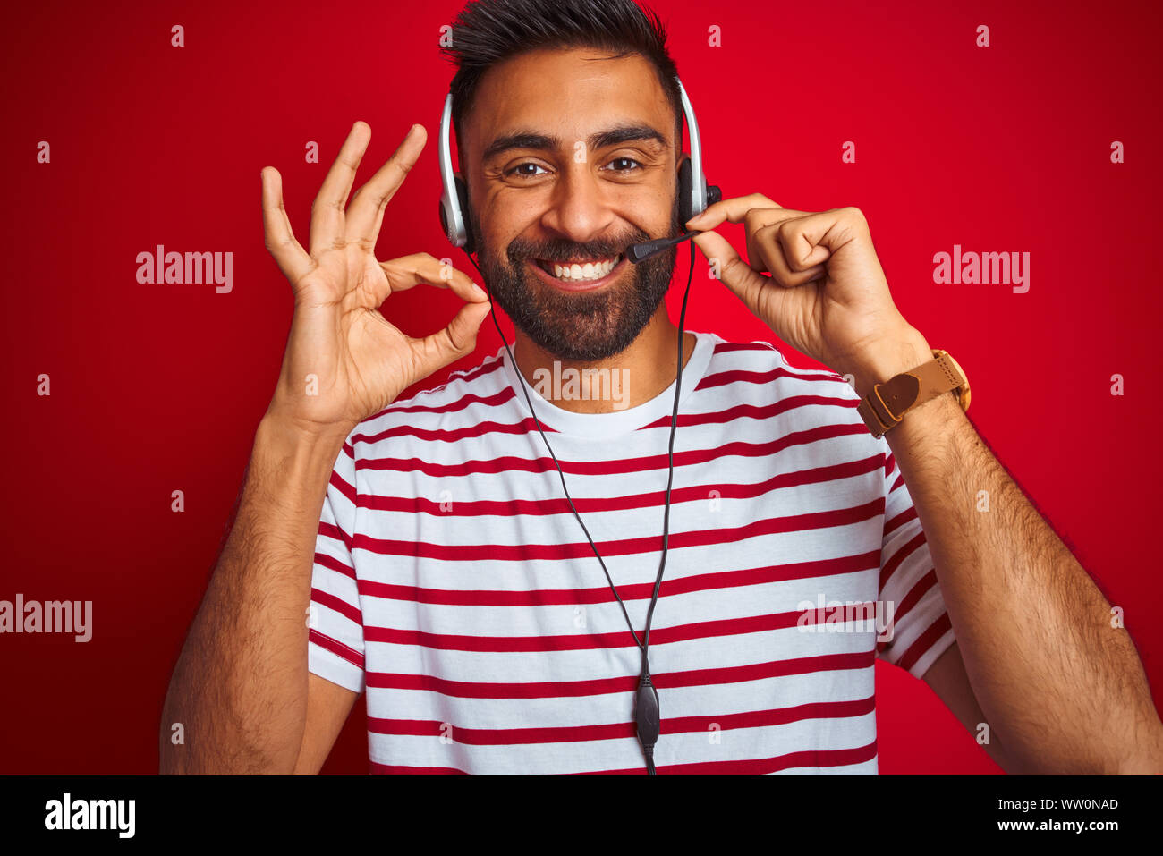 Young indian call center agent man using headset over isolated red ...