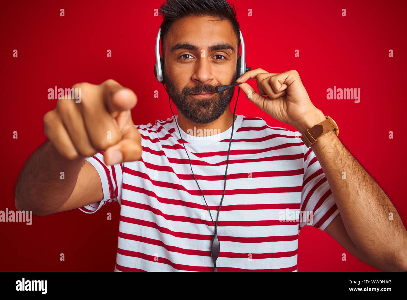Young indian call center agent man using headset over isolated red ...