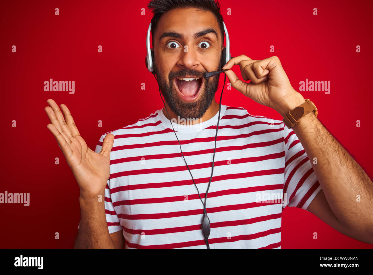 Young indian call center agent man using headset over isolated red ...