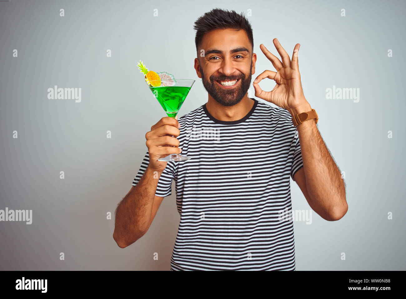 Young indian man drinking cocktail with alcohol standing over isolated ...
