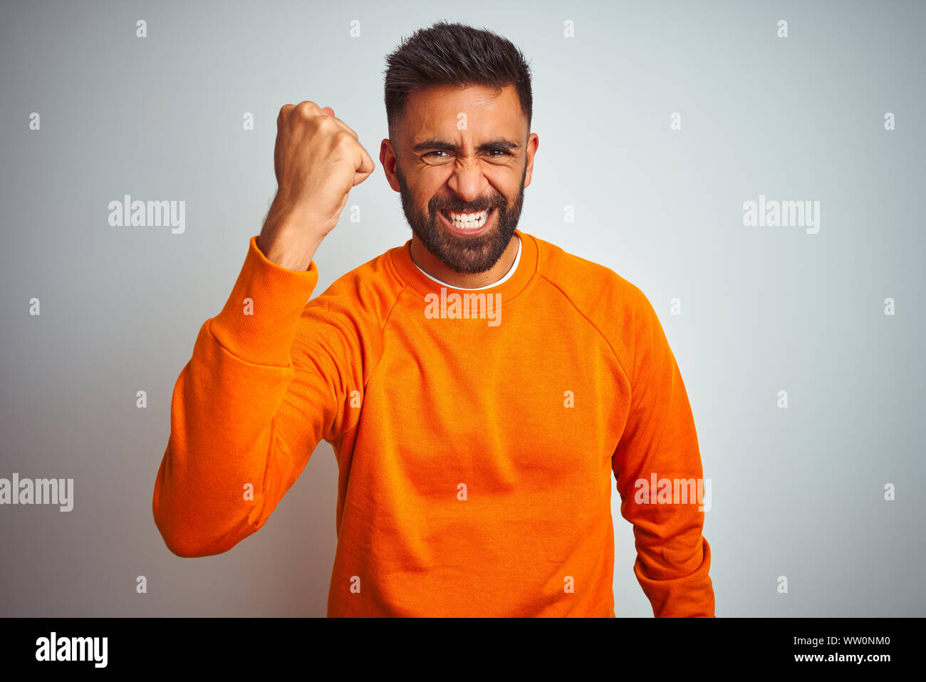 Young indian man wearing orange sweater over isolated white background ...