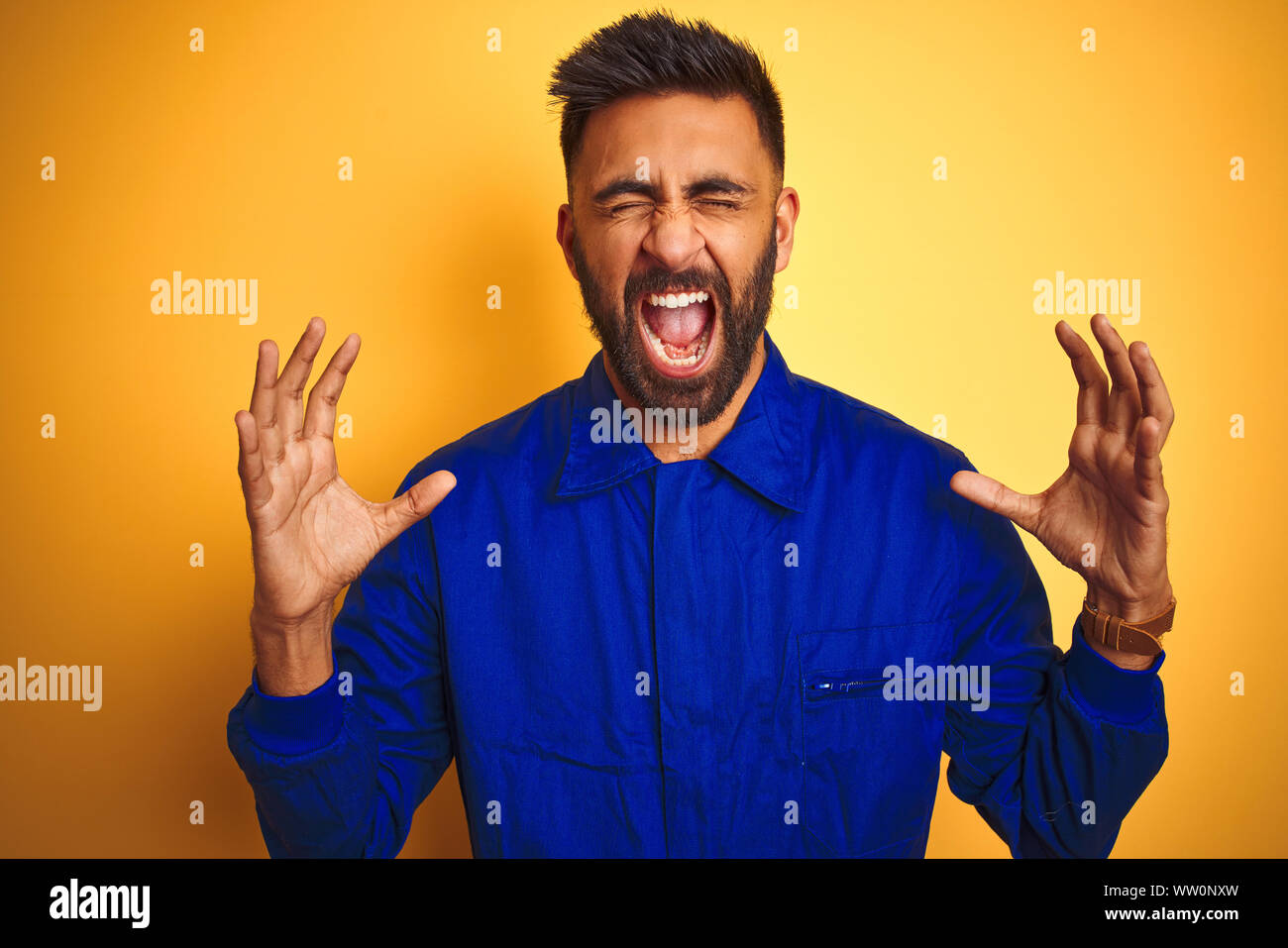 Handsome indian worker man wearing uniform over isolated yellow ...
