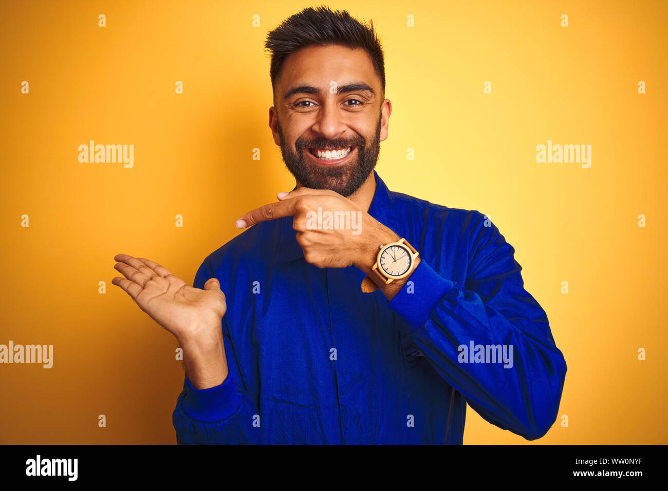 Handsome indian worker man wearing uniform over isolated yellow ...
