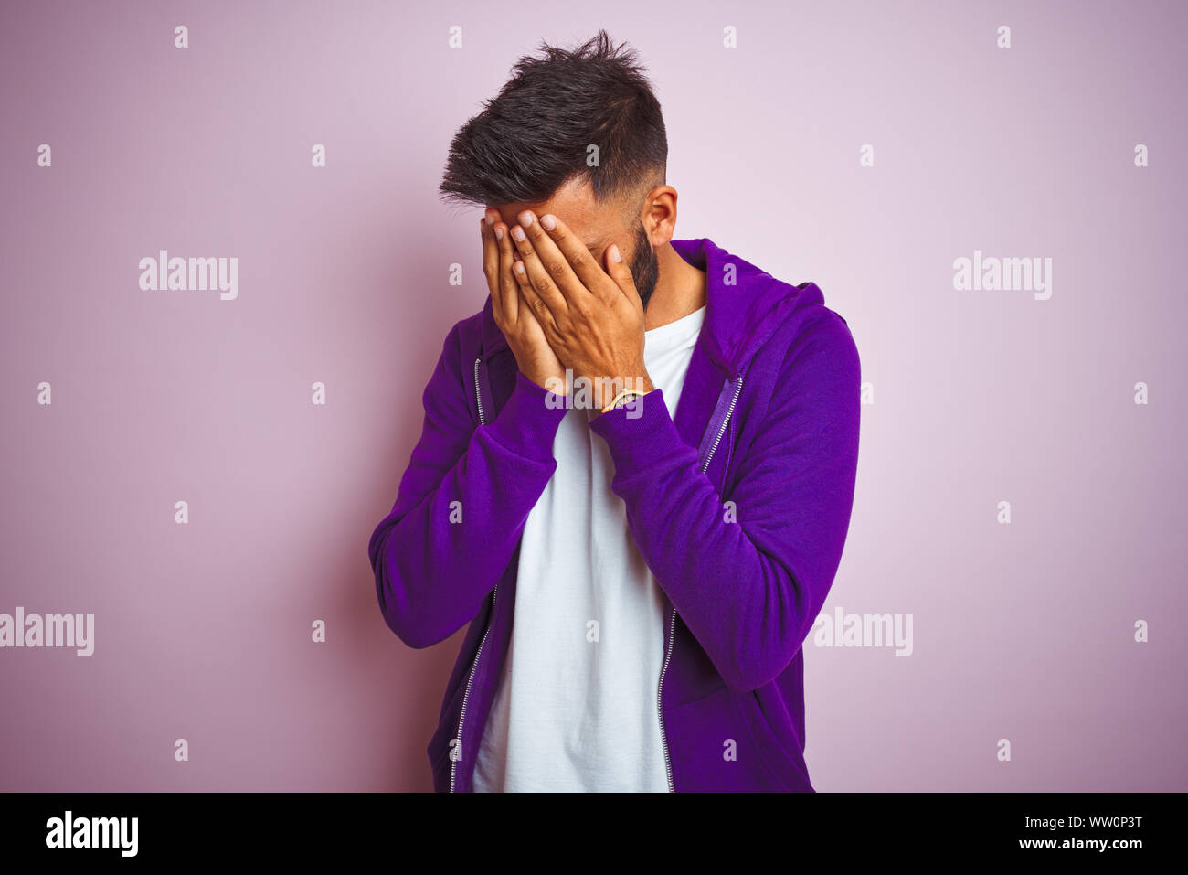 Young indian man wearing purple sweatshirt standing over isolated pink ...