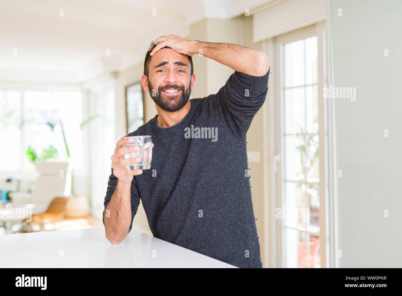 Handsome hispanic man drinking a fresh glass of water stressed with ...