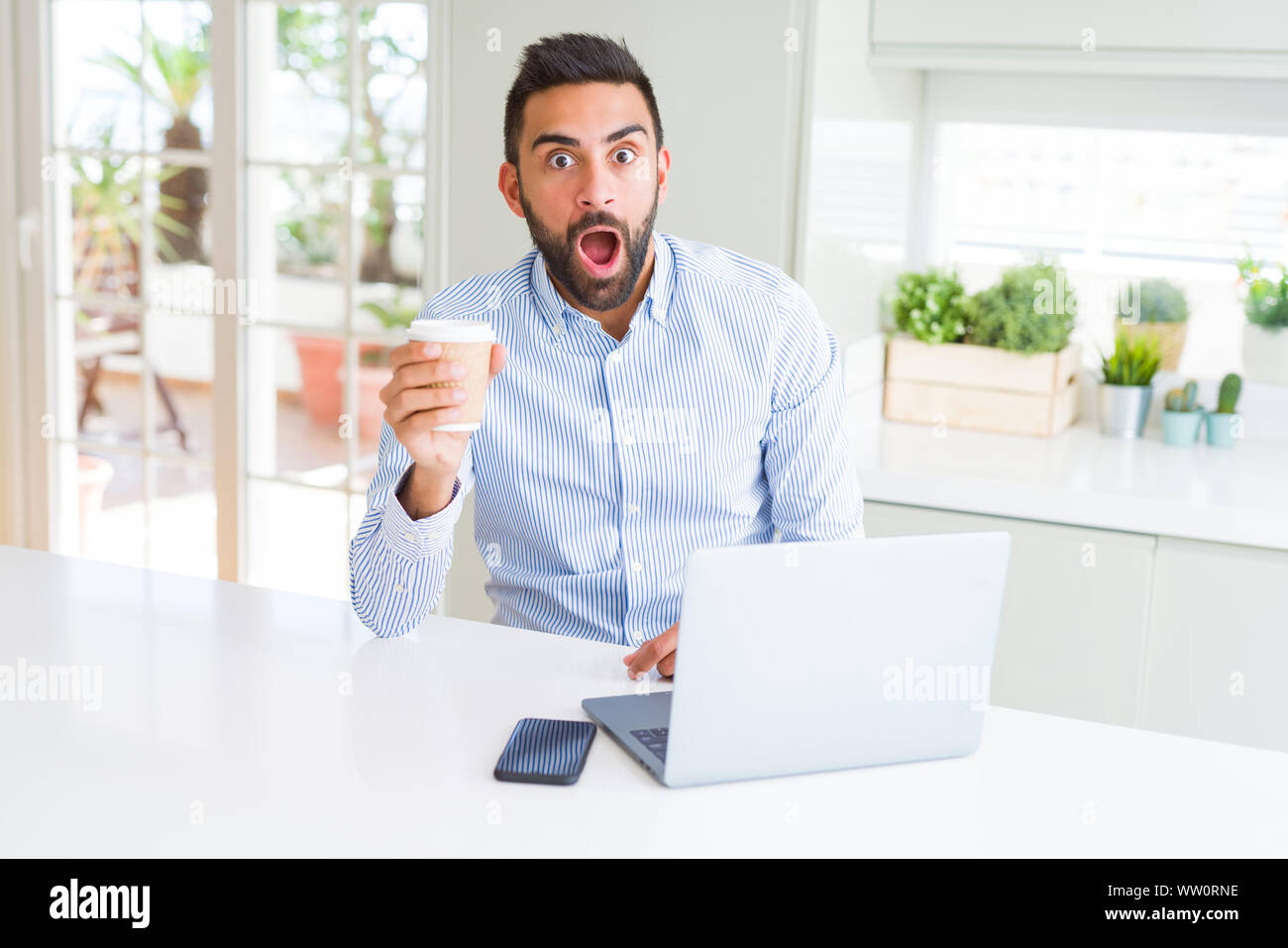 Handsome hispanic man working using computer laptop and drinking a cup ...