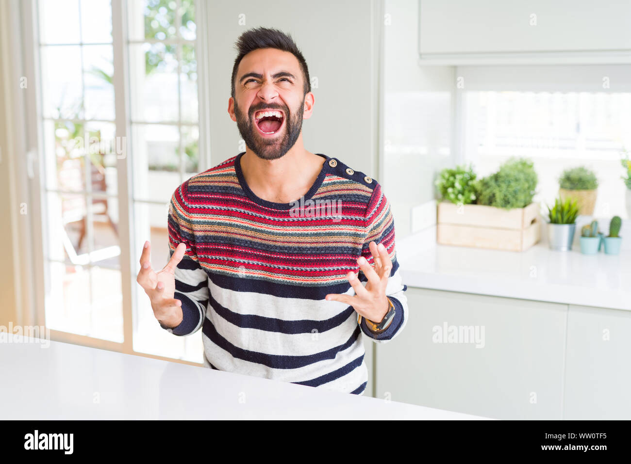 Handsome hispanic man wearing stripes sweater at home crazy and mad ...