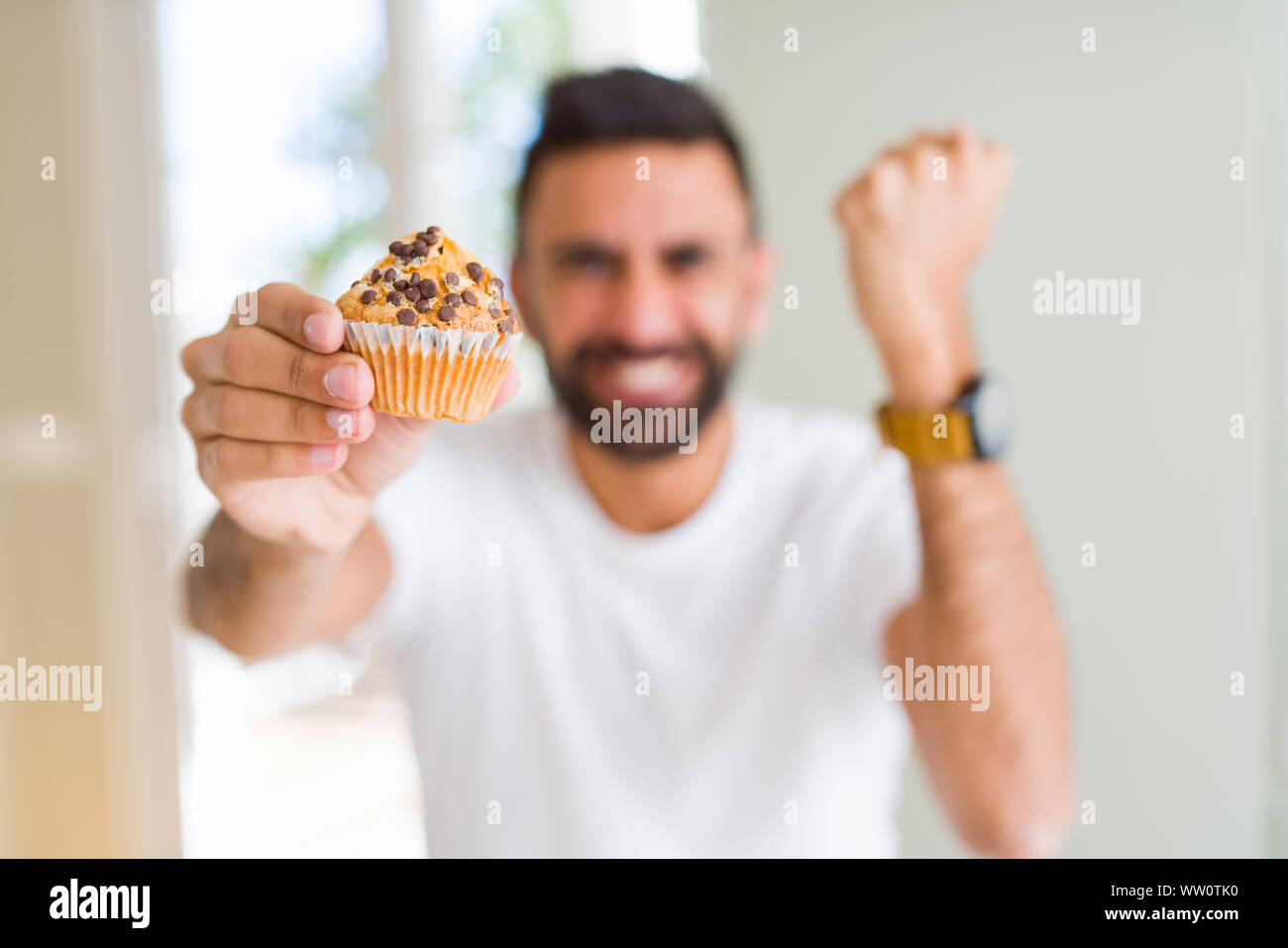 Handsome hispanic man eating chocolate chips muffin annoyed and ...