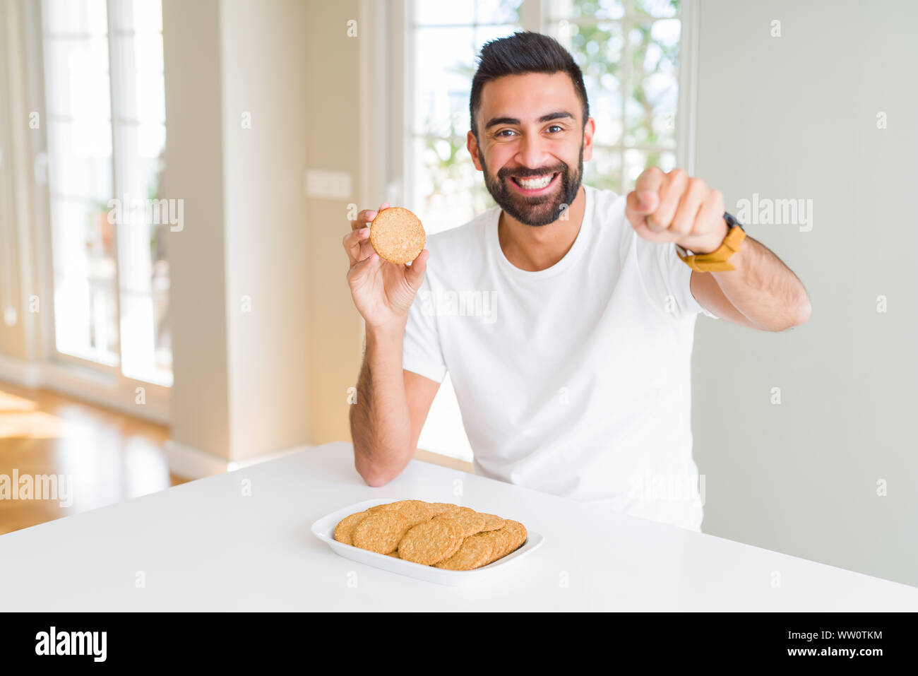 Handsome hispanic man eating healthy whole grain biscuits pointing with ...