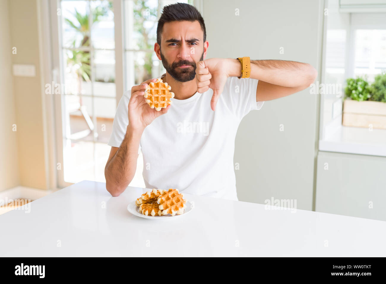 Handsome hispanic man eating sweet belgian waffle pastry with angry ...