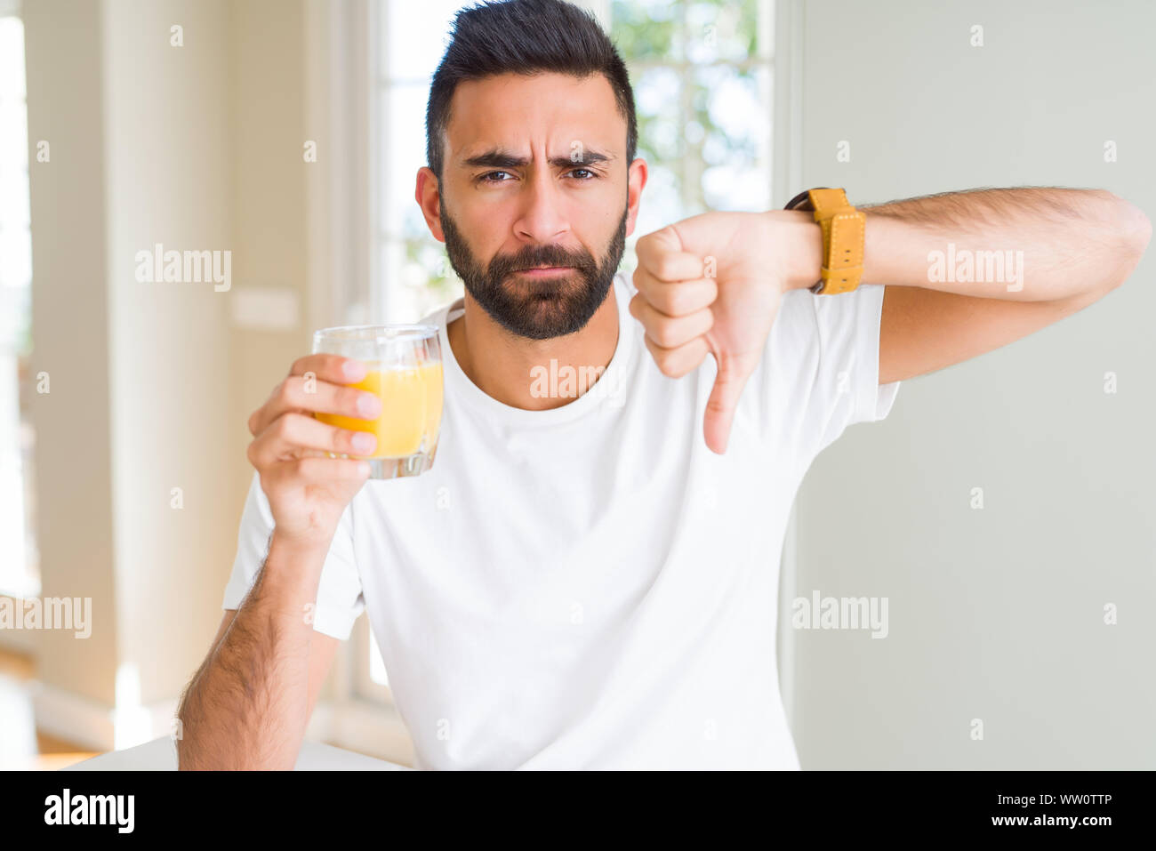 Handsome hispanic man drinking healthy orange juice with angry face ...