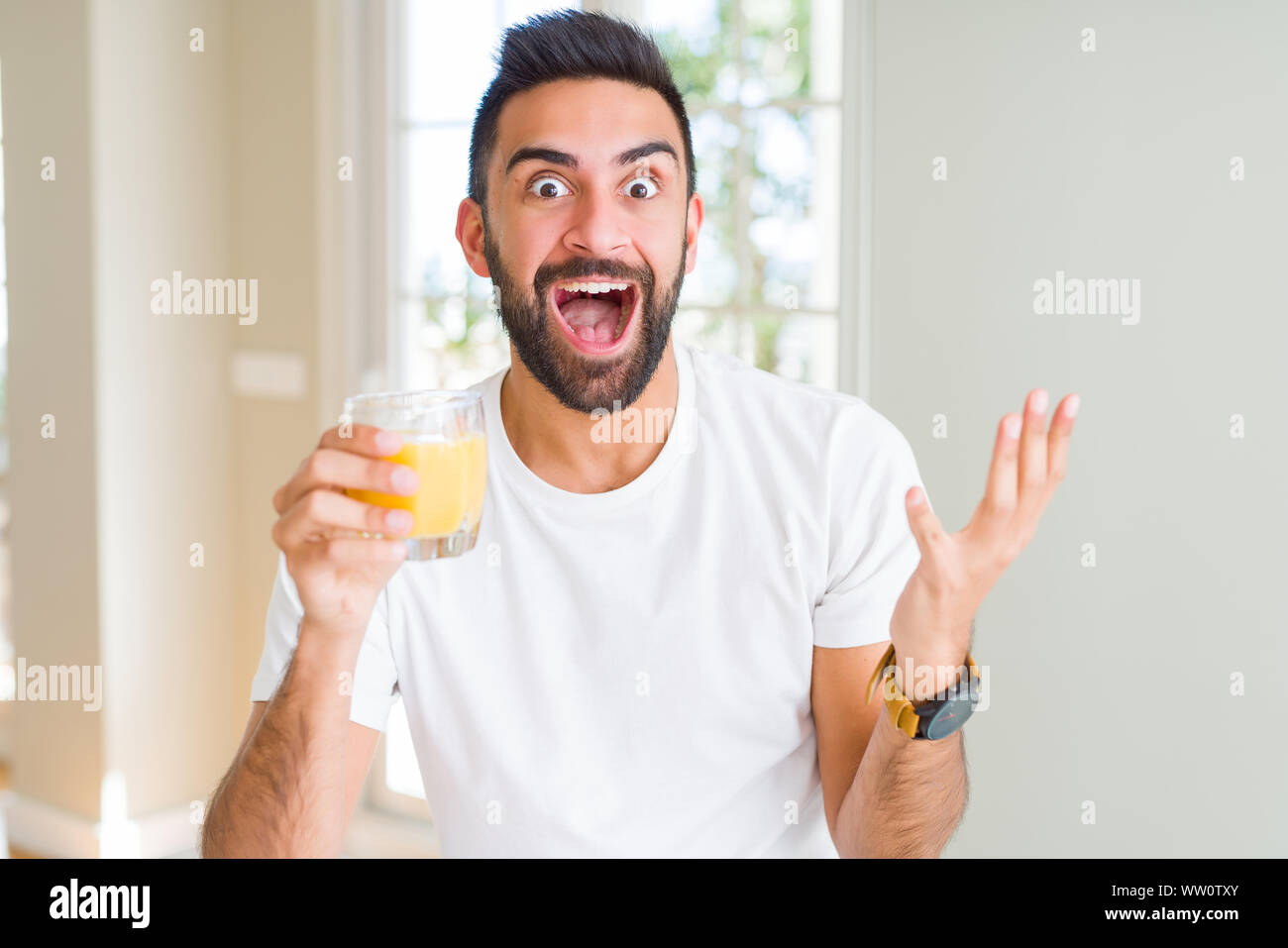 Handsome hispanic man drinking healthy orange juice very happy and ...
