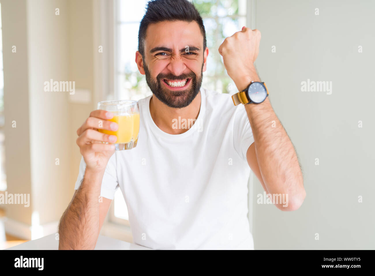 Handsome hispanic man drinking healthy orange juice annoyed and ...