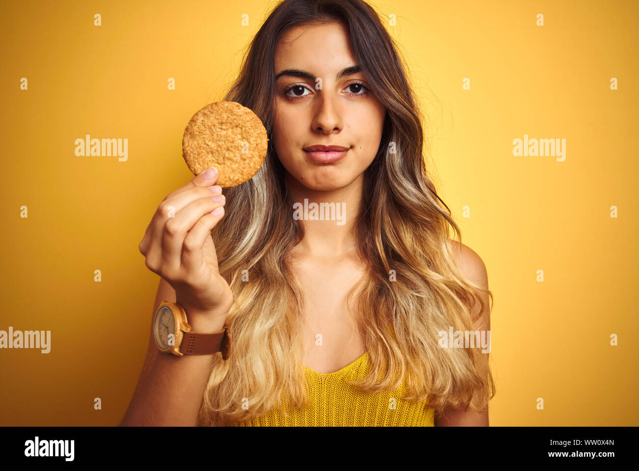 Young beautiful woman eating biscuit over grey isolated background with ...