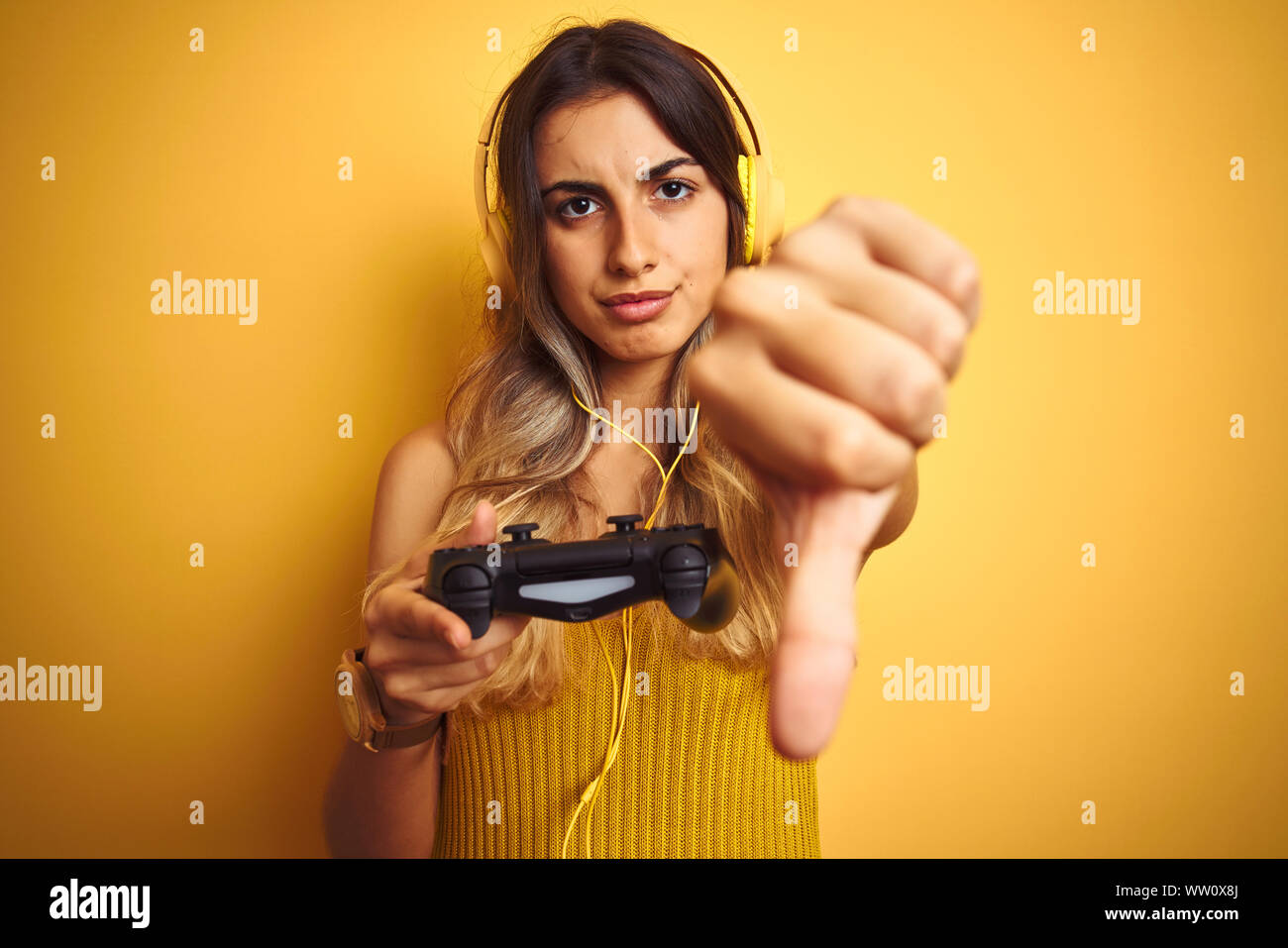 Young beautiful woman playing video game using gamepad over yellow ...