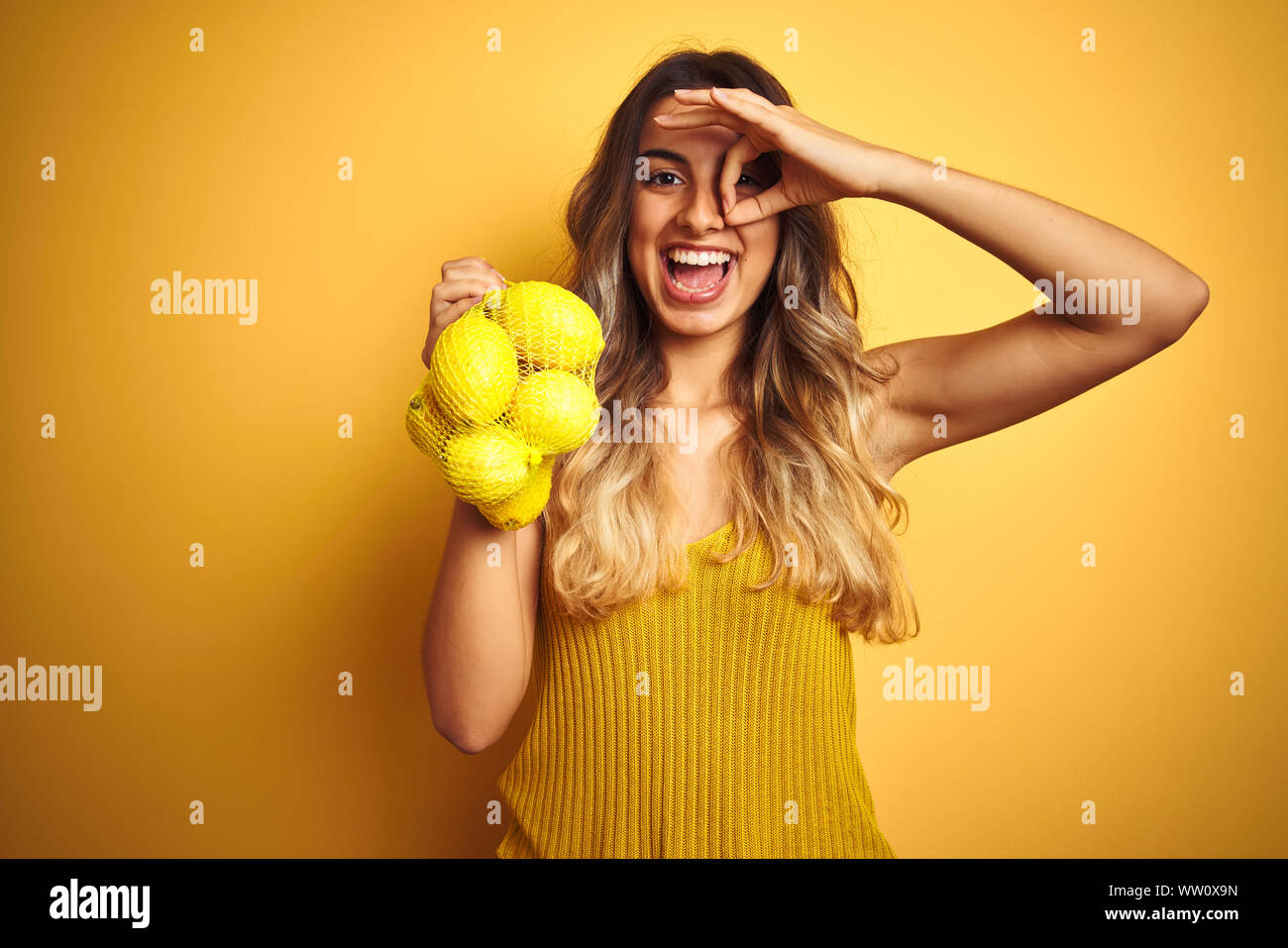 Young beautiful woman holding net of lemons over yellow isolated ...