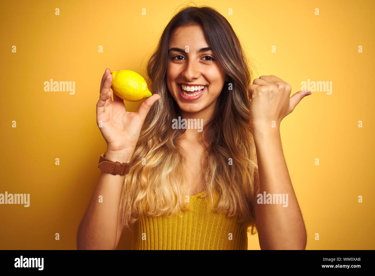 Young beautiful woman eating a lemon over yellow isolated background ...