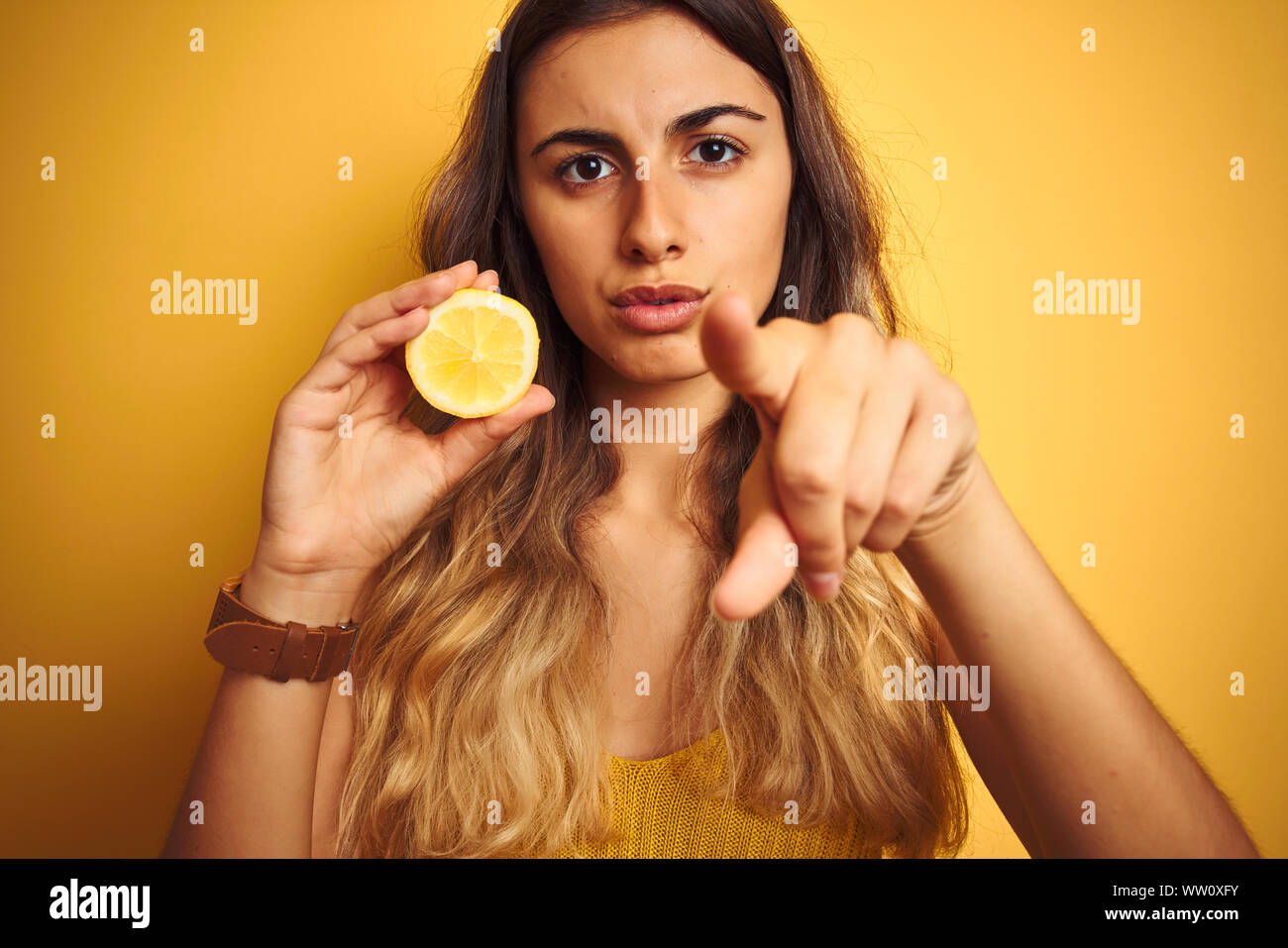 Young beautiful woman holding half lemon over yellow isolated ...