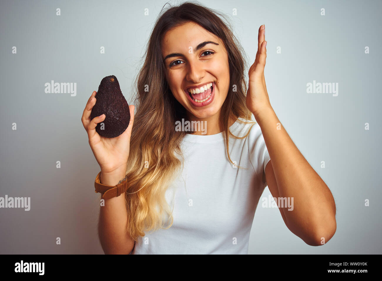 Young beautiful woman eating avocado over grey isolated background very ...