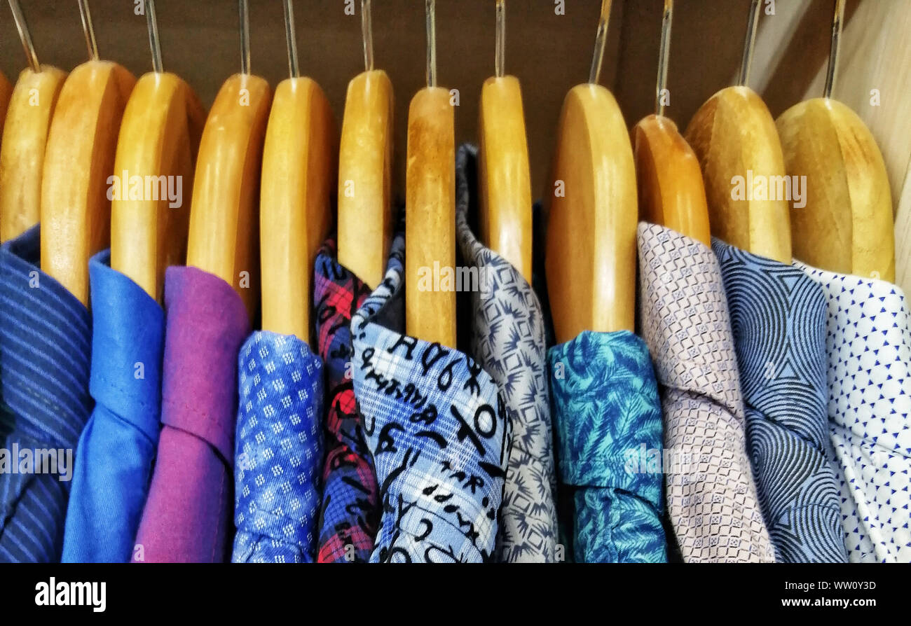 a row of wooden hangers with shirts of different colors and prints ...