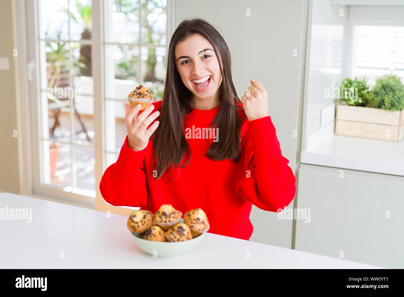 Beautiful young woman eating chocolate chips muffins screaming proud ...
