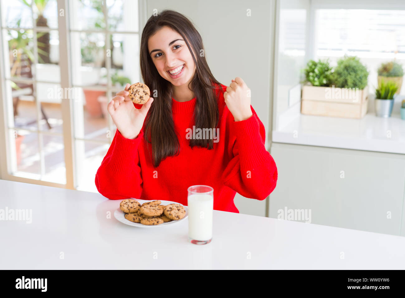 Beautiful young woman eating chocolate chips cookies and glass of milk ...