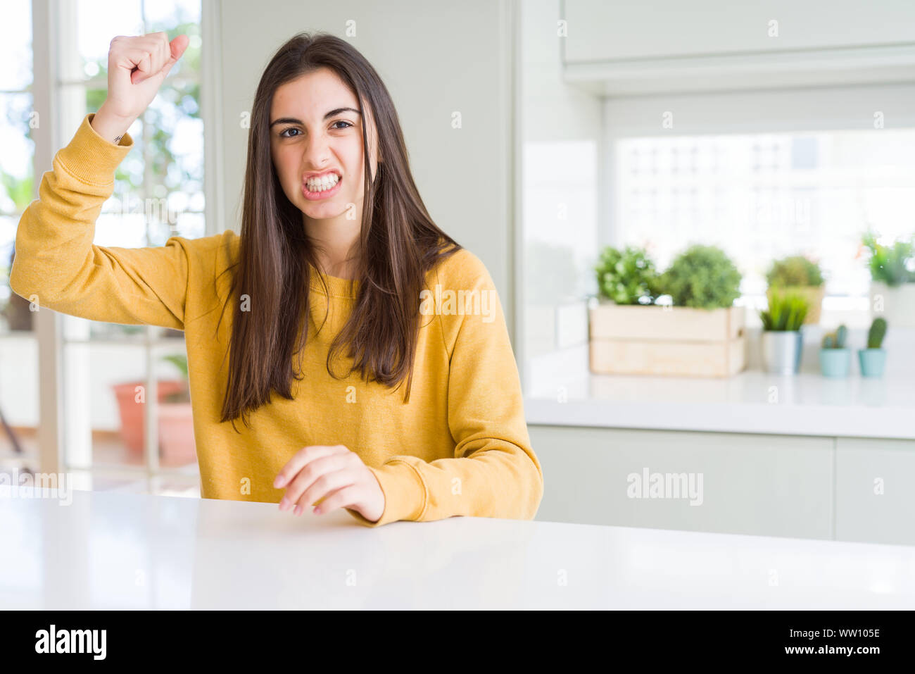 Beautiful young woman wearing yellow sweater angry and mad raising fist ...