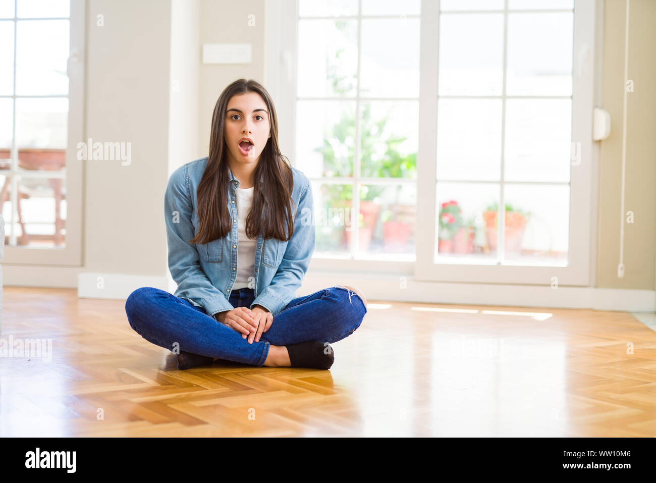 Beautiful young woman sitting on the floor at home afraid and shocked ...