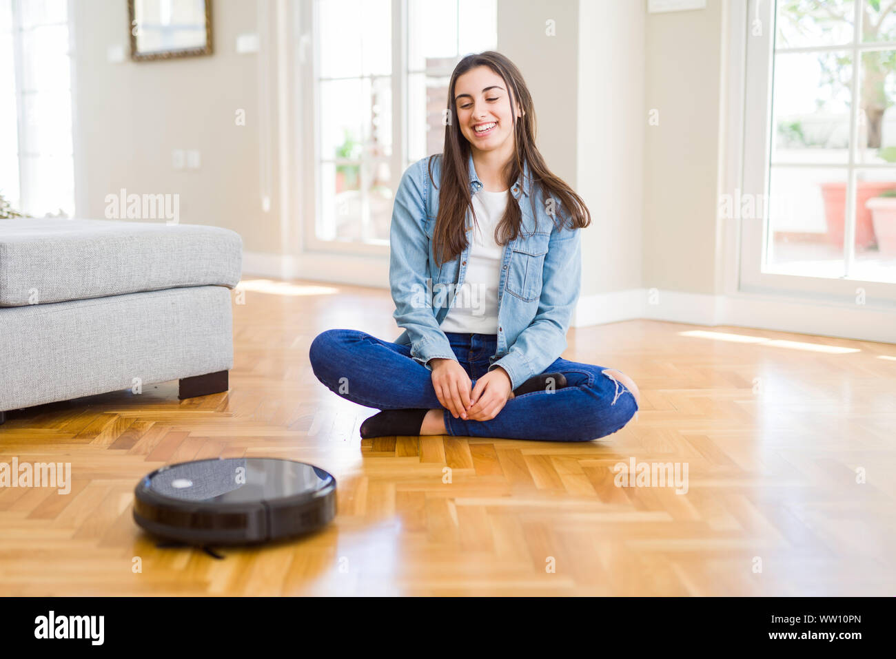 Young woman using automatic vacuum cleaner to clean the floor ...