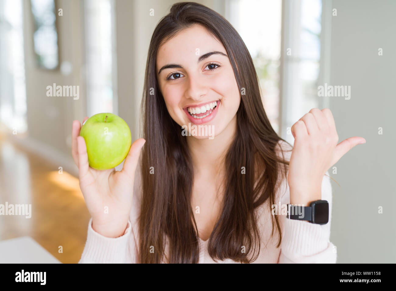 Beautiful young woman eating healthy green apple fruit pointing and ...
