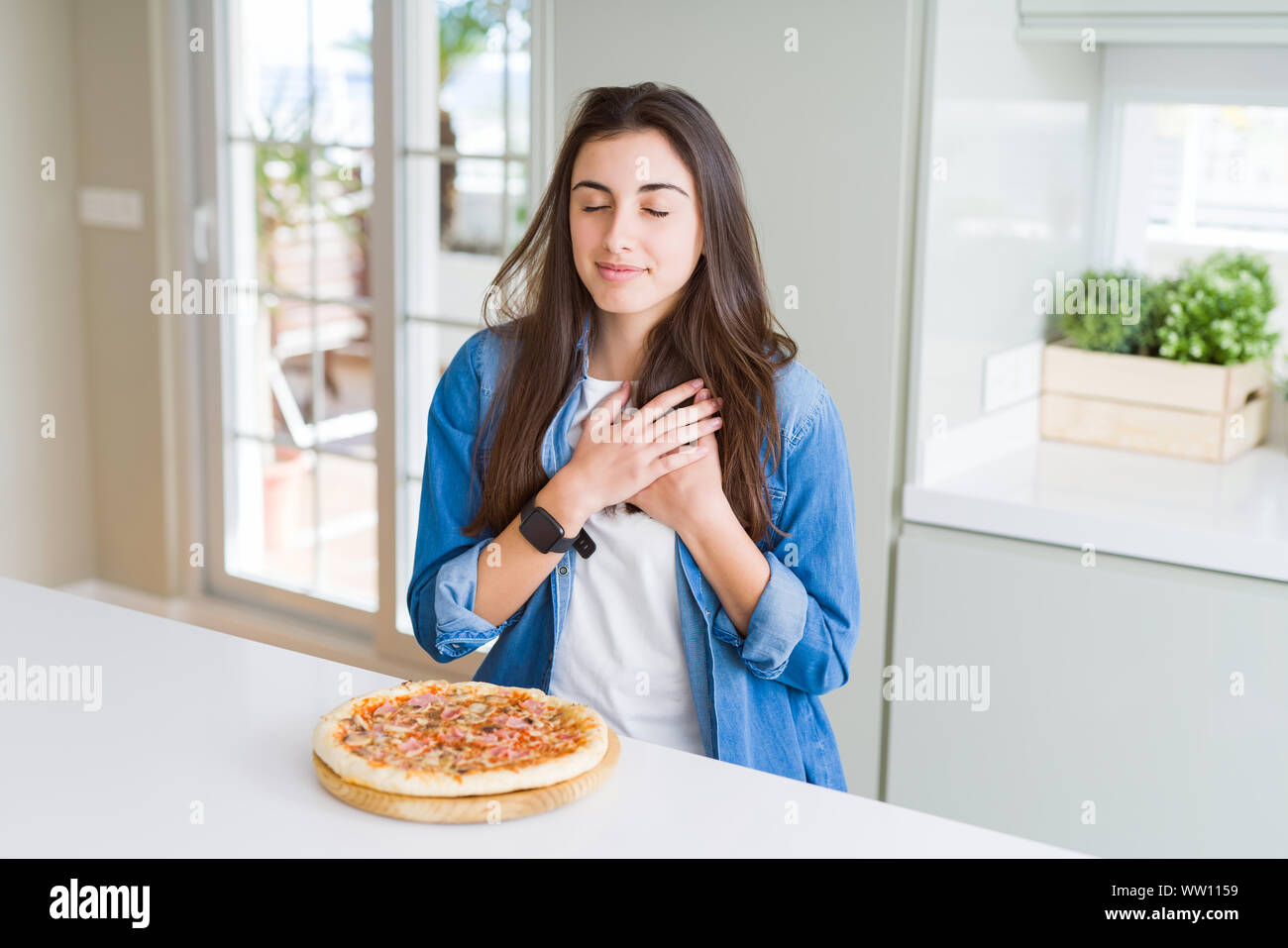 Beautiful young woman eating homemade tasty pizza at the kitchen ...