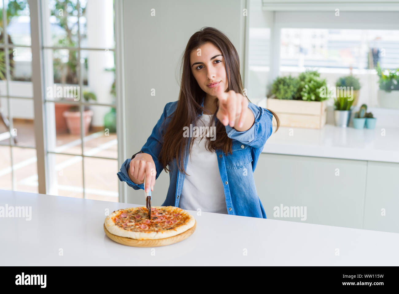 Beautiful young woman cutting a tasty pizza slice using a cutter ...