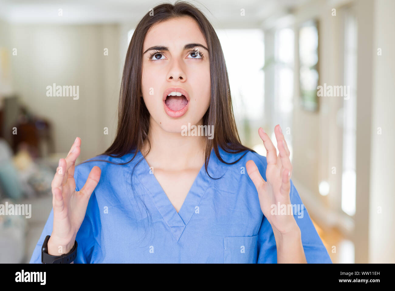 Beautiful young nurse woman at the clinic crazy and mad shouting and ...