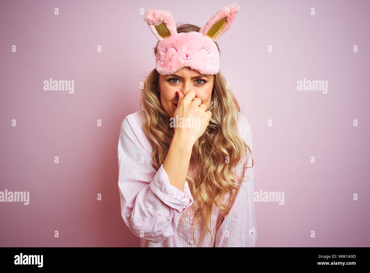 Young beautiful woman wearing pajama and sleep mask over pink isolated ...