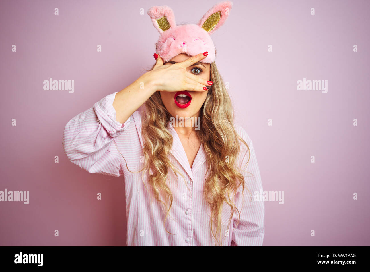 Young beautiful woman wearing pajama and sleep mask over pink isolated ...